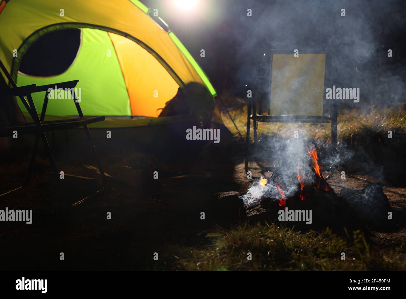 Smoking bonfire and folding chairs near camping tent outdoors in ...