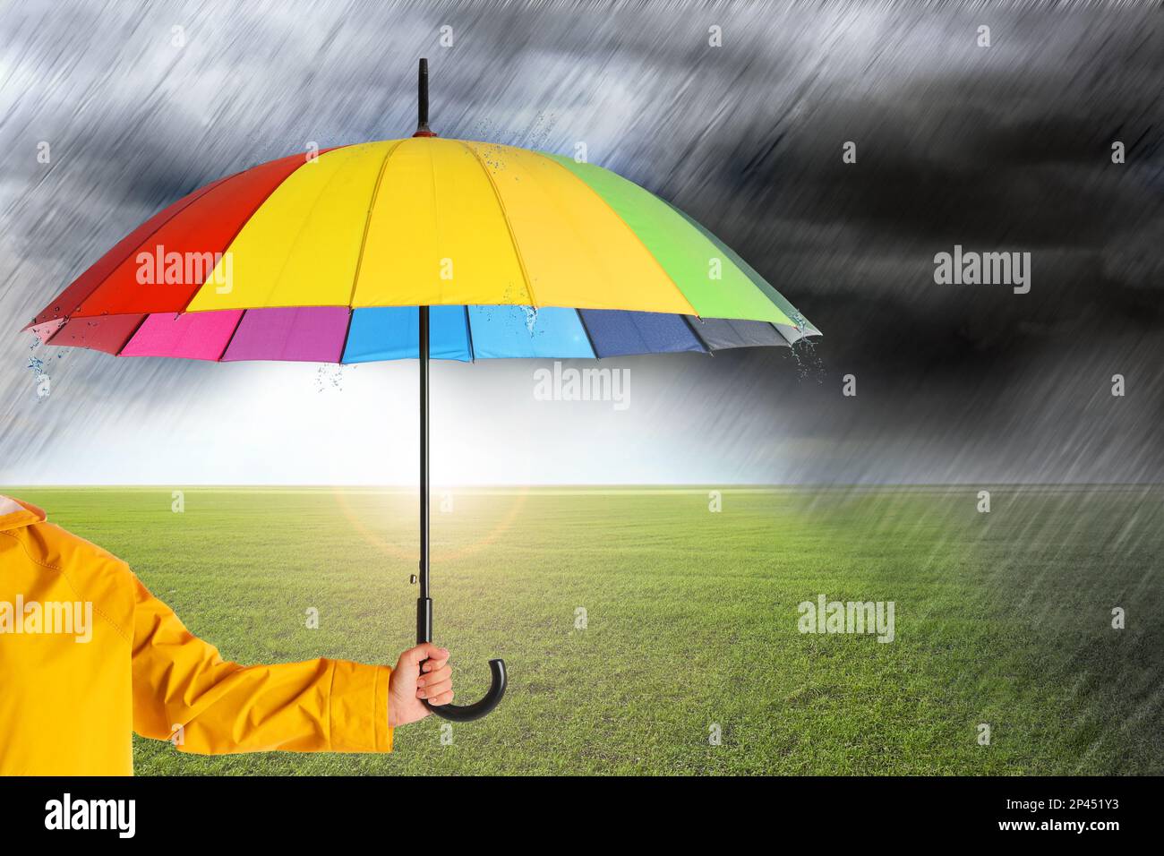 Woman with open bright umbrella under heavy rain in green field ...