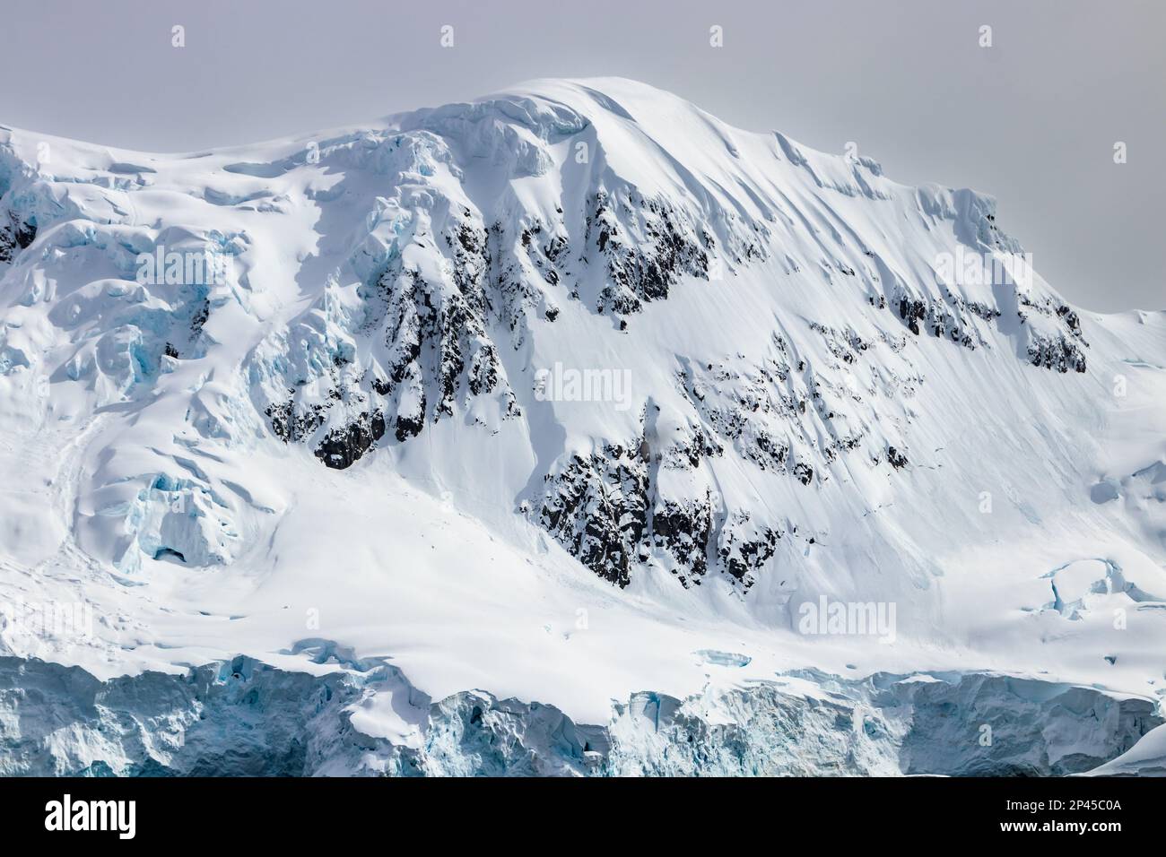 Snow covered mountain peak, Antarctic Peninsula. Rocks exposed on snowy ...