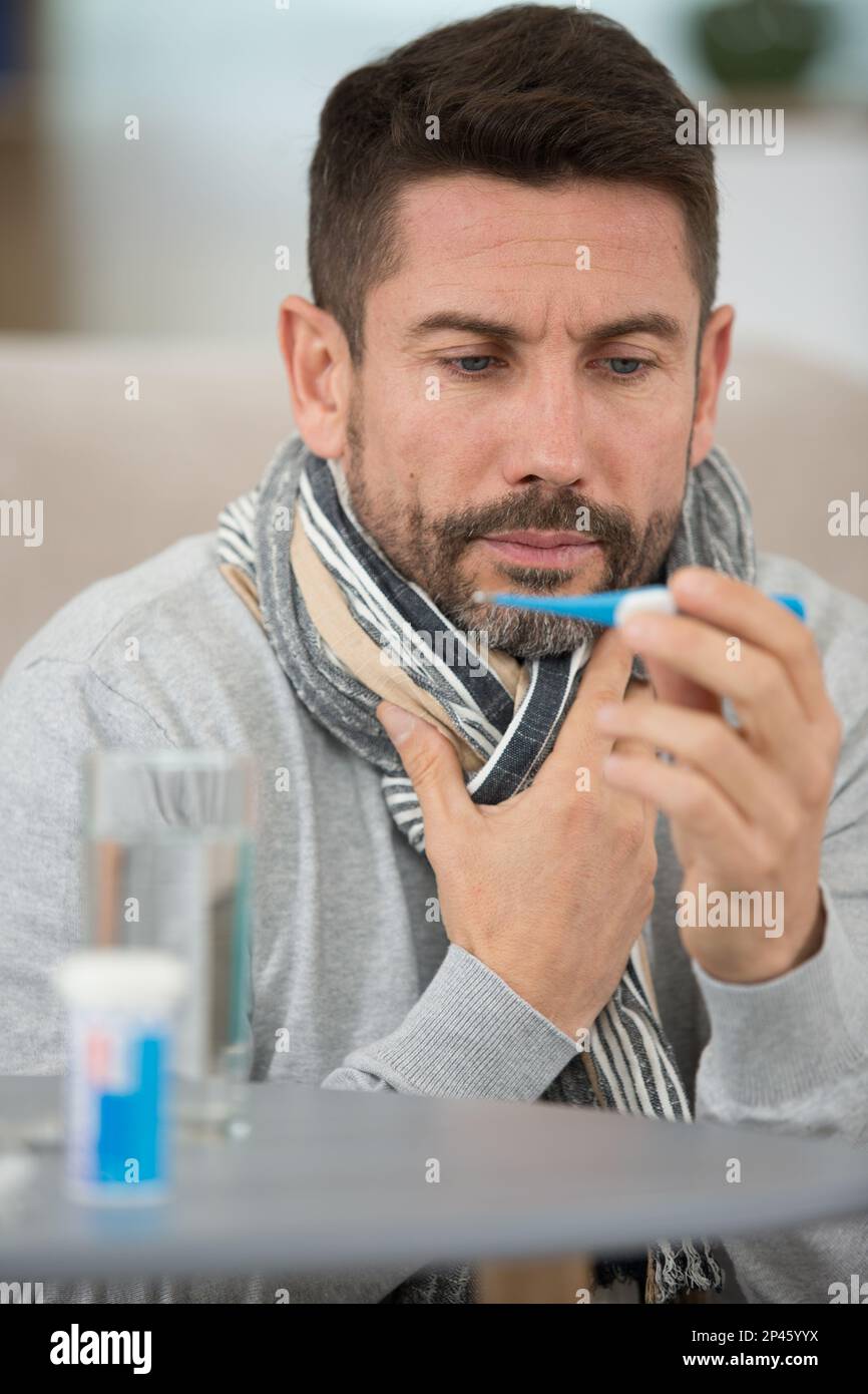 sick man lying on sofa checking his temperature at home Stock Photo - Alamy