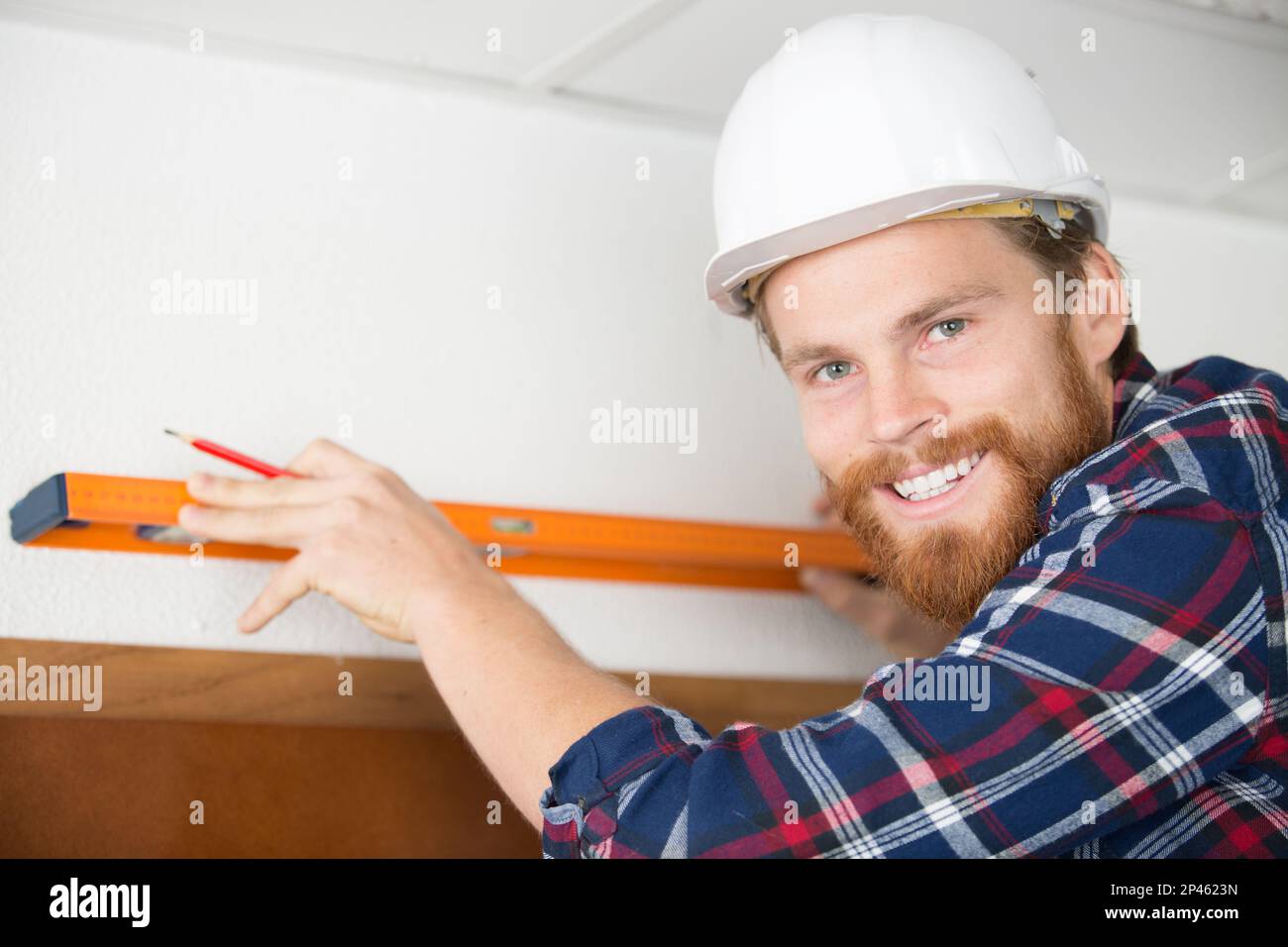 young man using spirit level on white wall Stock Photo - Alamy