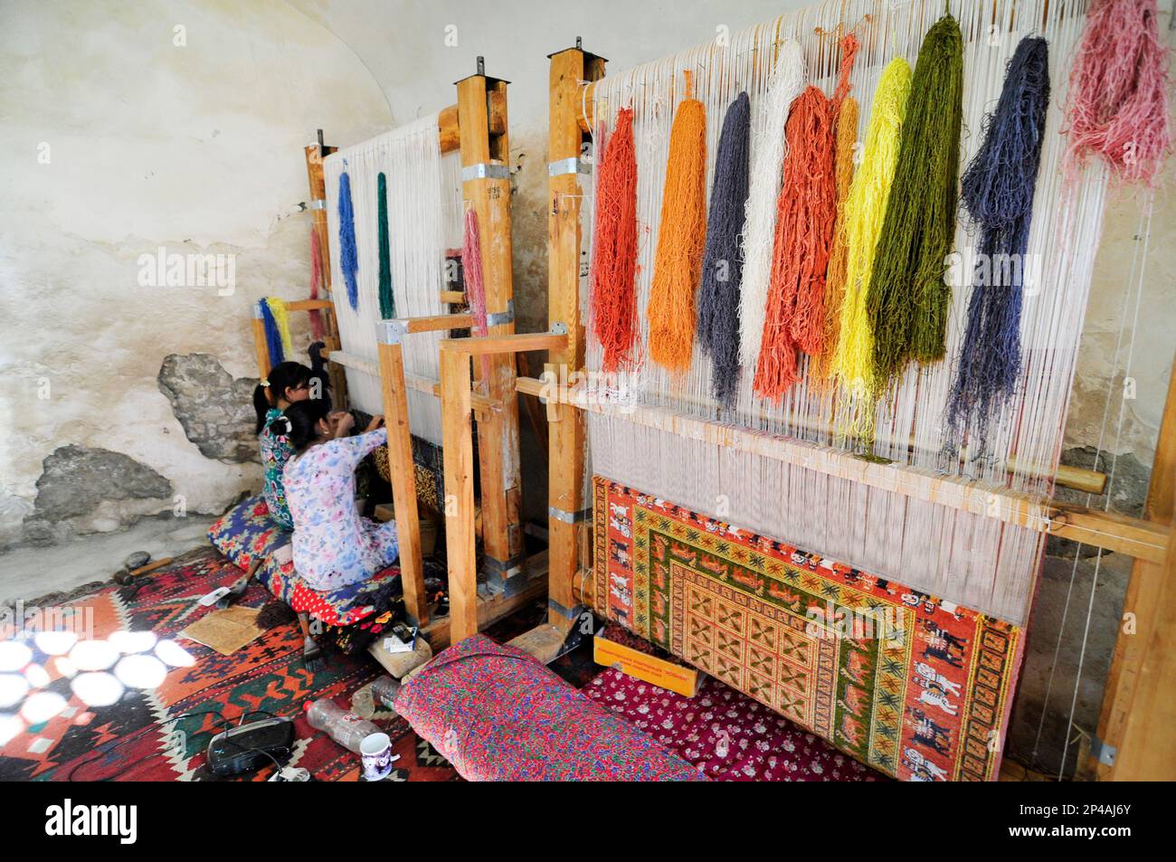 Uzbek women weaving a handmade traditional carpet in a small rug ...
