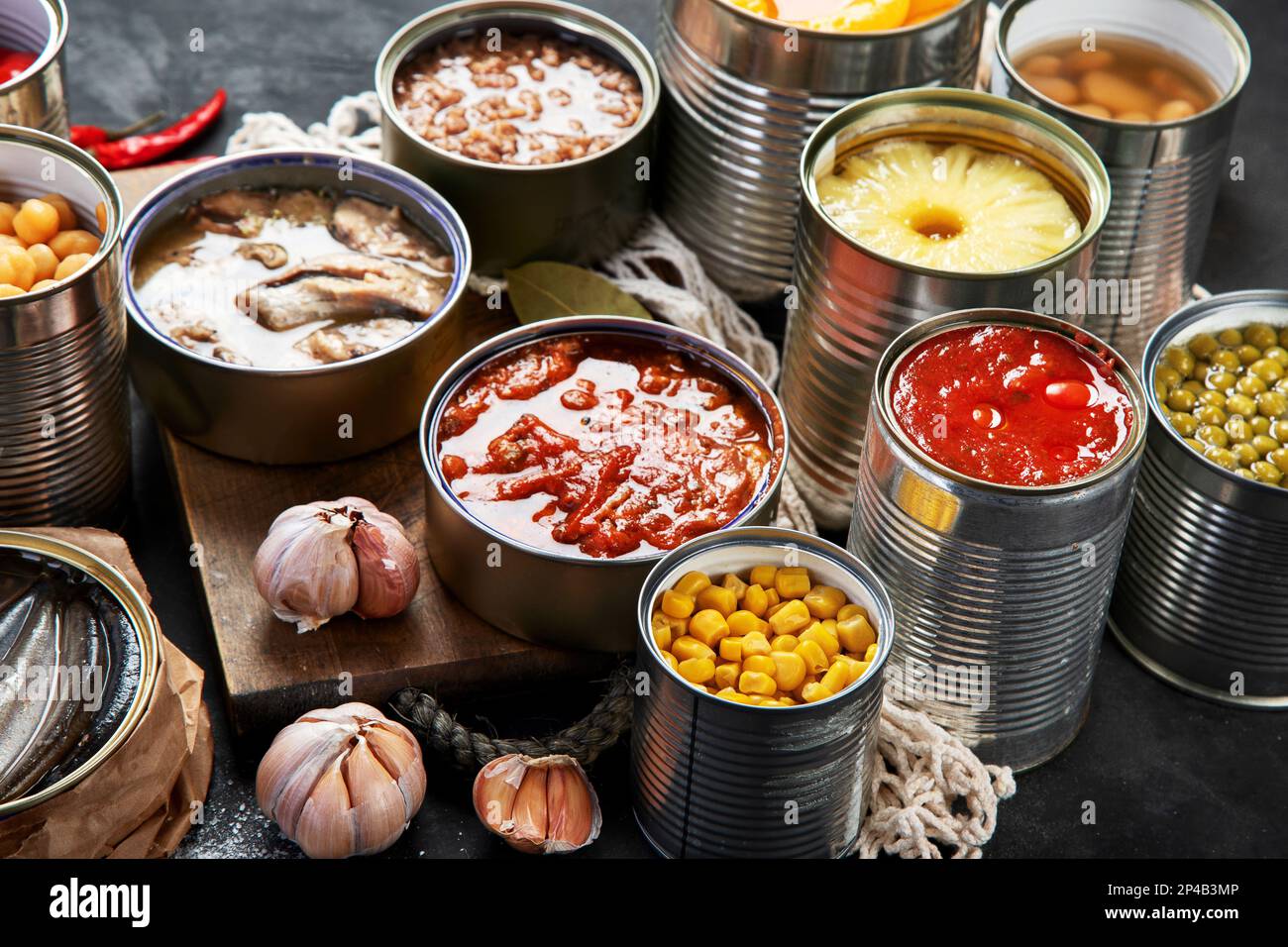 Various canned vegetables, meat, fish and fruits in tin cans. On a dark ...