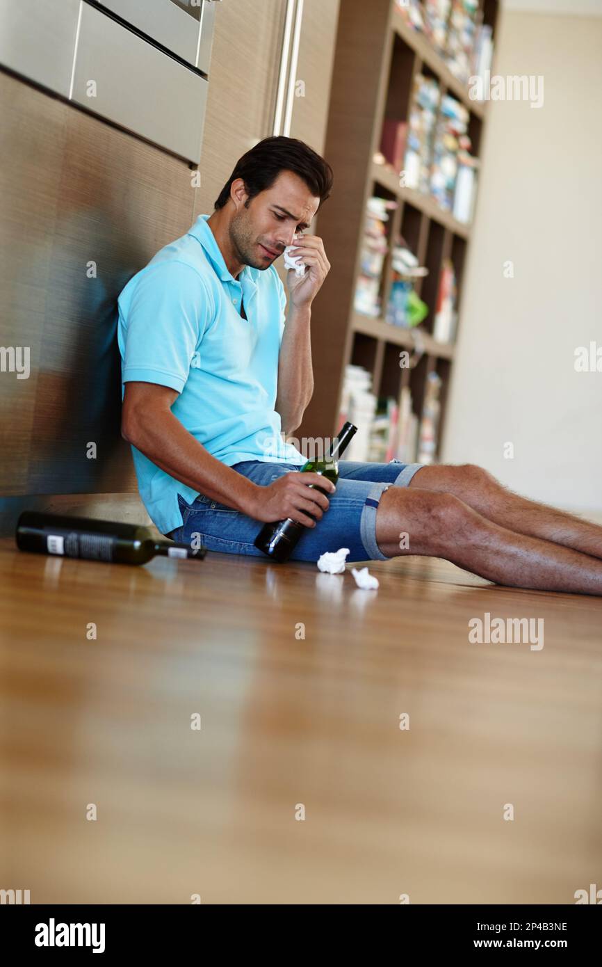 Hes inconsolable. a crying man drinking wine while sitting on the floor ...