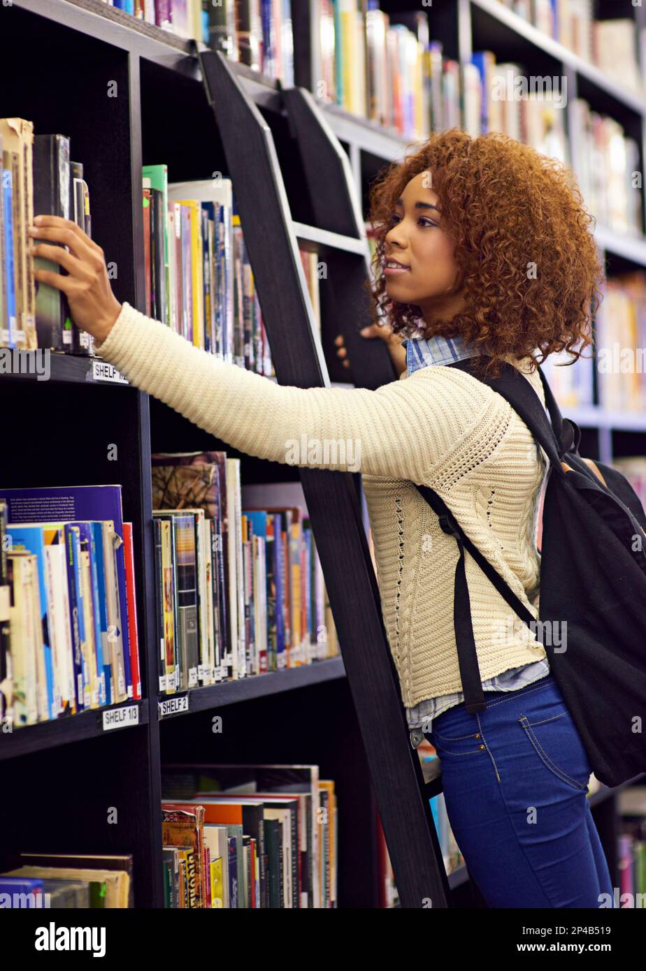Seeking knowledge in the library. a young woman reaching for a book ...