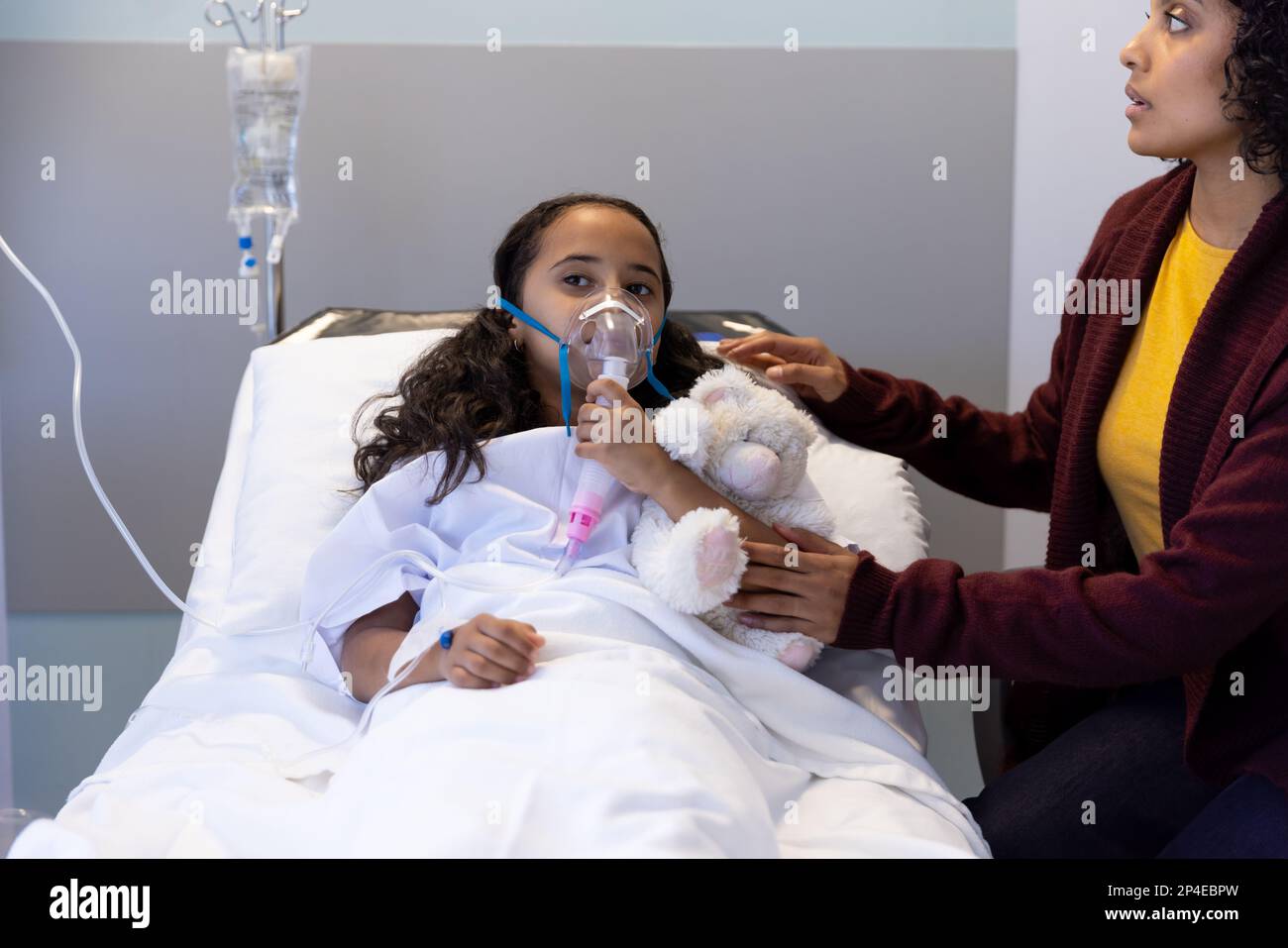 Biracial mother and sick daughter with oxygen mask and teddy bear on ...