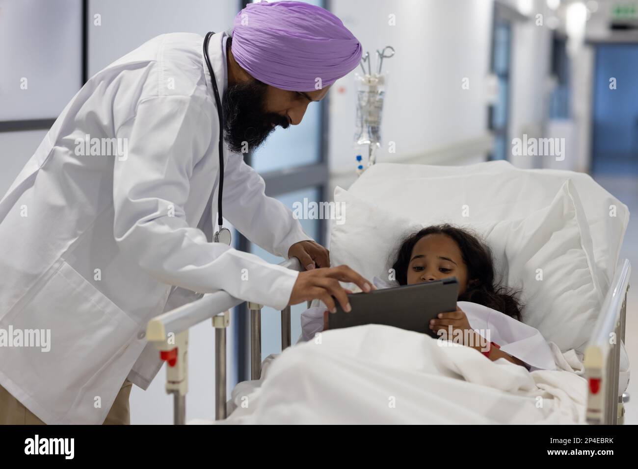 Sikh male doctor in turban with girl using tablet and lying on hospital ...