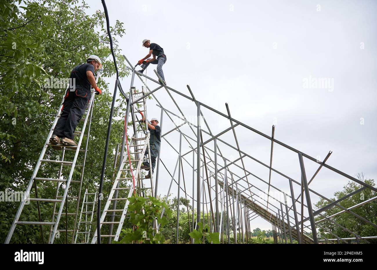 Three men in workwear installing metal poles and rails for photovoltaic ...