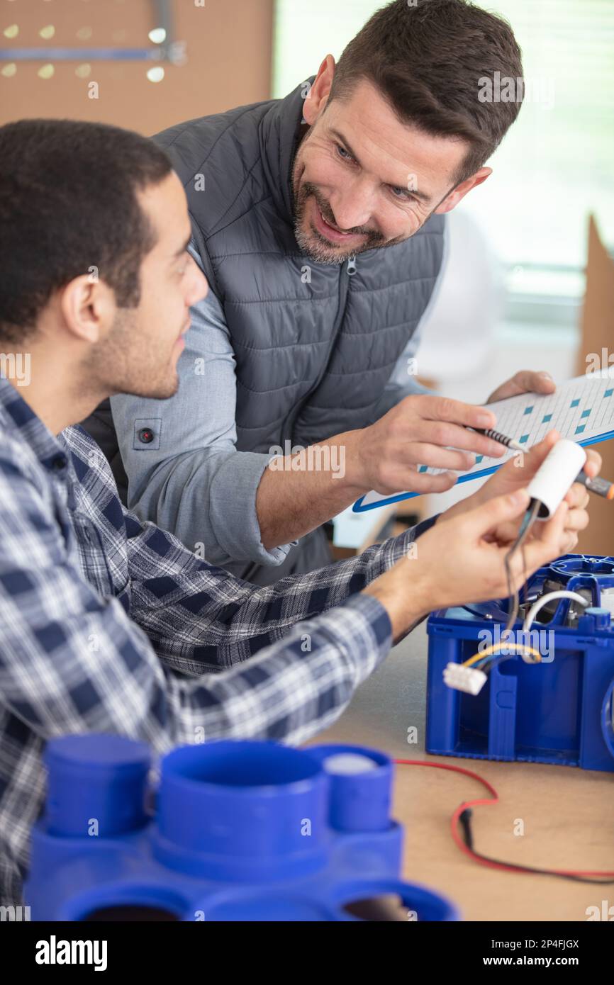 apprentice in workshop assembles ventilation system with his mentor ...
