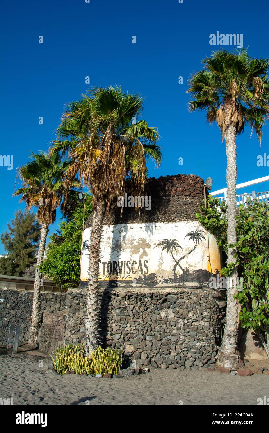 Torviscas Playa lettering on a stone wall on the beach, with palm trees ...