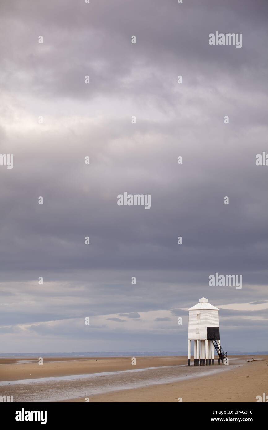 Rain clouds and low wooden pole lighthouse on the beach at low tide ...