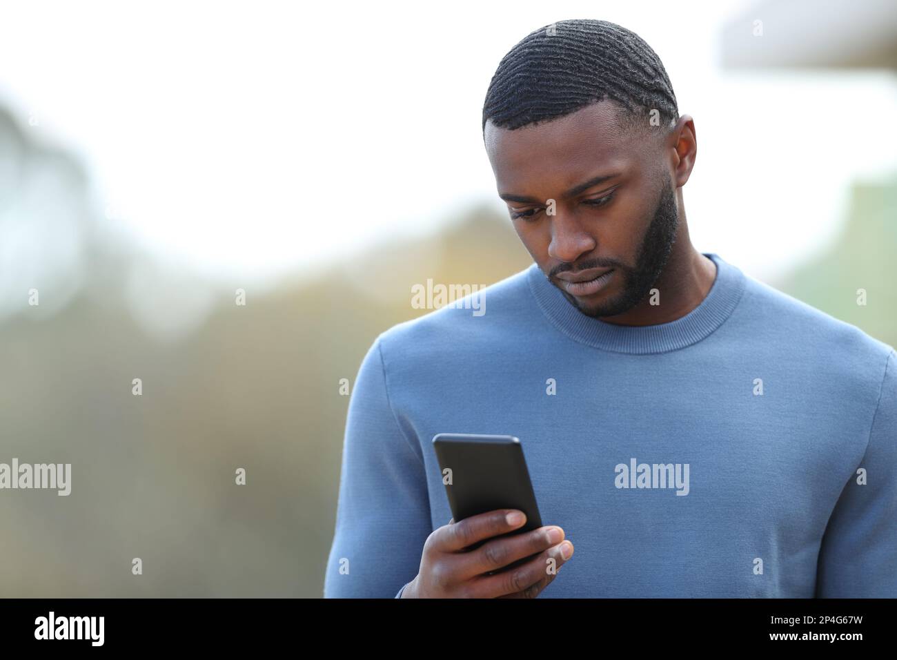 Sad black man reading chat on phone in the street Stock Photo - Alamy