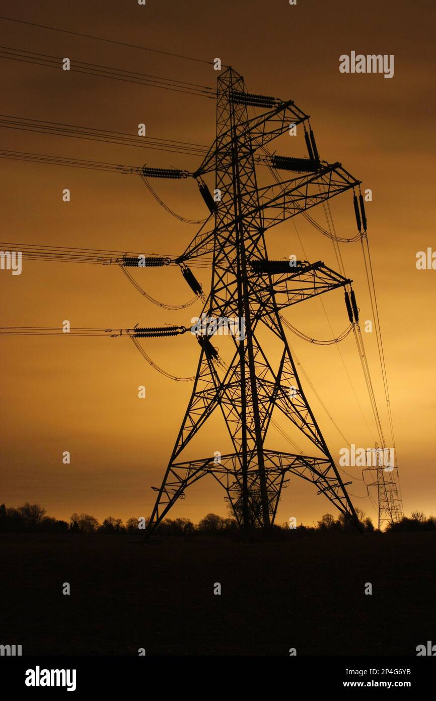 Electricity pylon and overhead power lines illuminated at night by ...