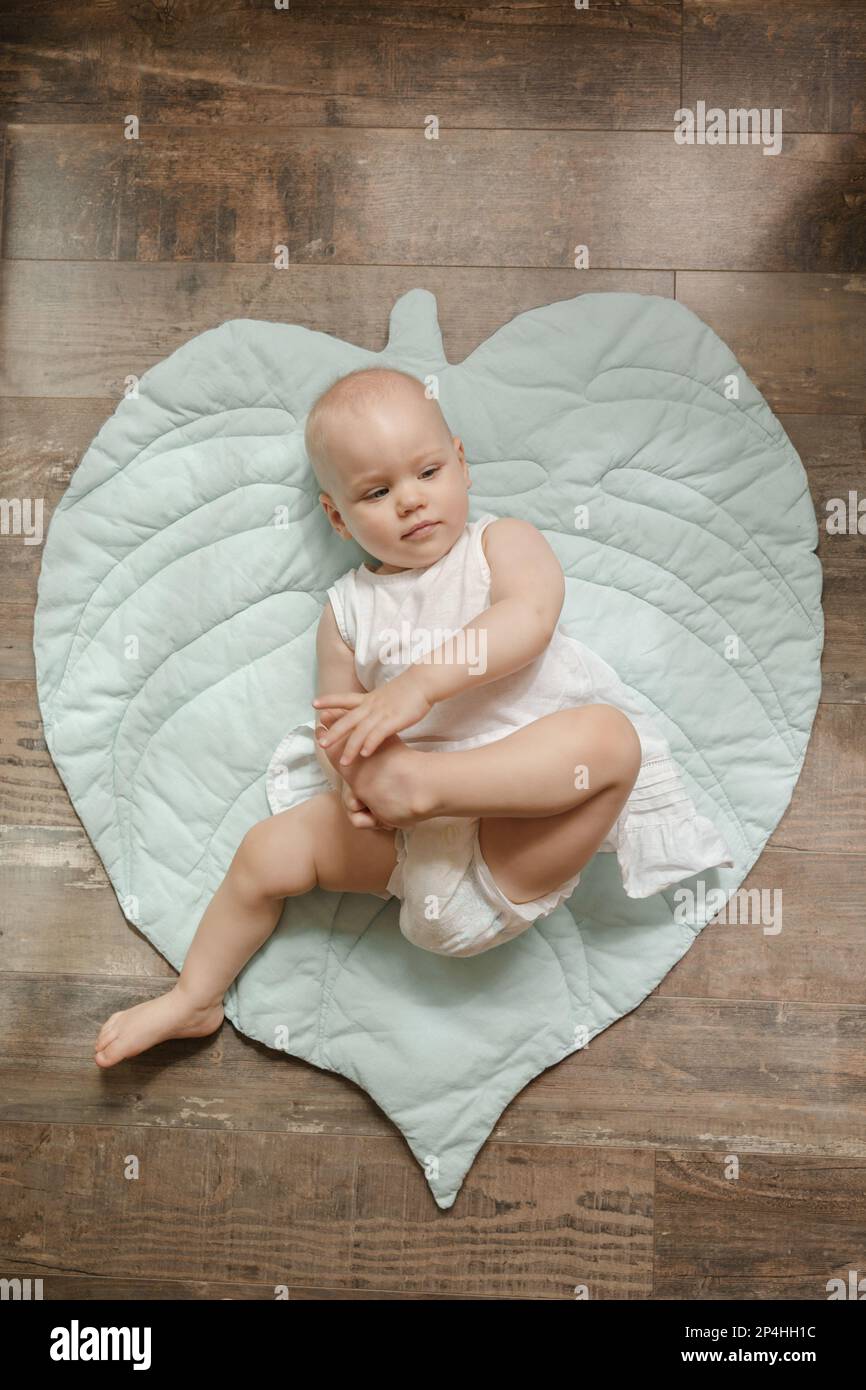 Bald baby girl in a white linen dress with gypsophila on a leaf rug ...