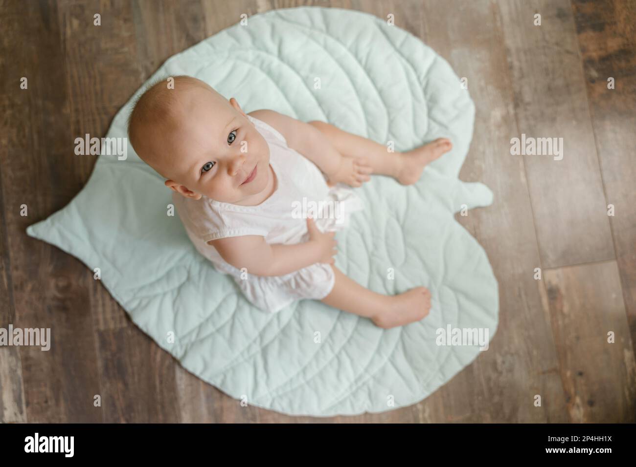 Bald baby girl in a white linen dress with gypsophila on a leaf rug ...