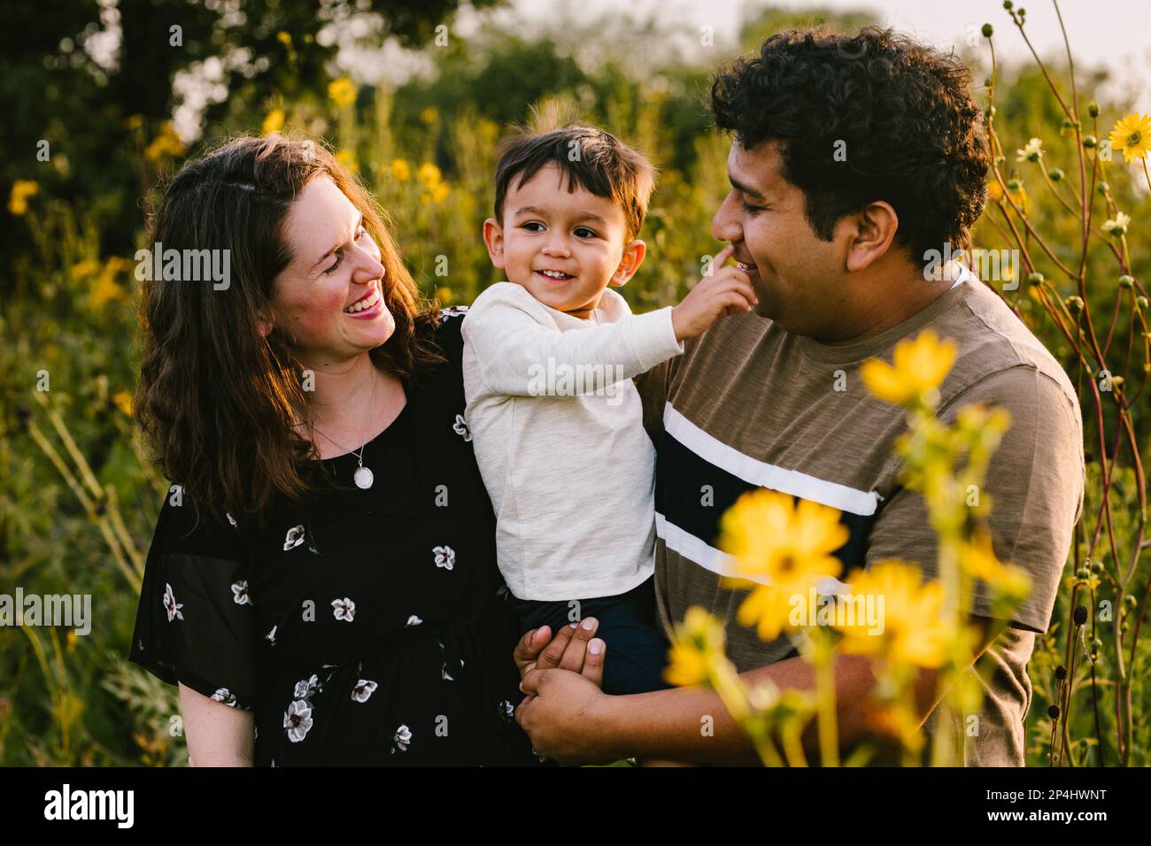 Latino dad and mom laugh with toddler son in flower field Stock Photo ...