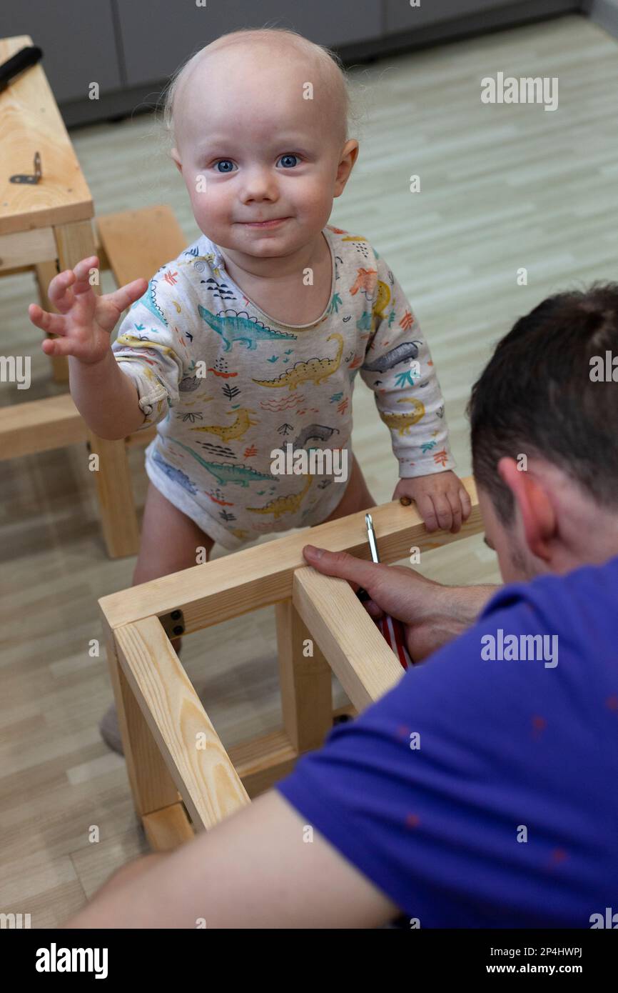 Smiling blue eyed child stands near father building wooden chair Stock ...