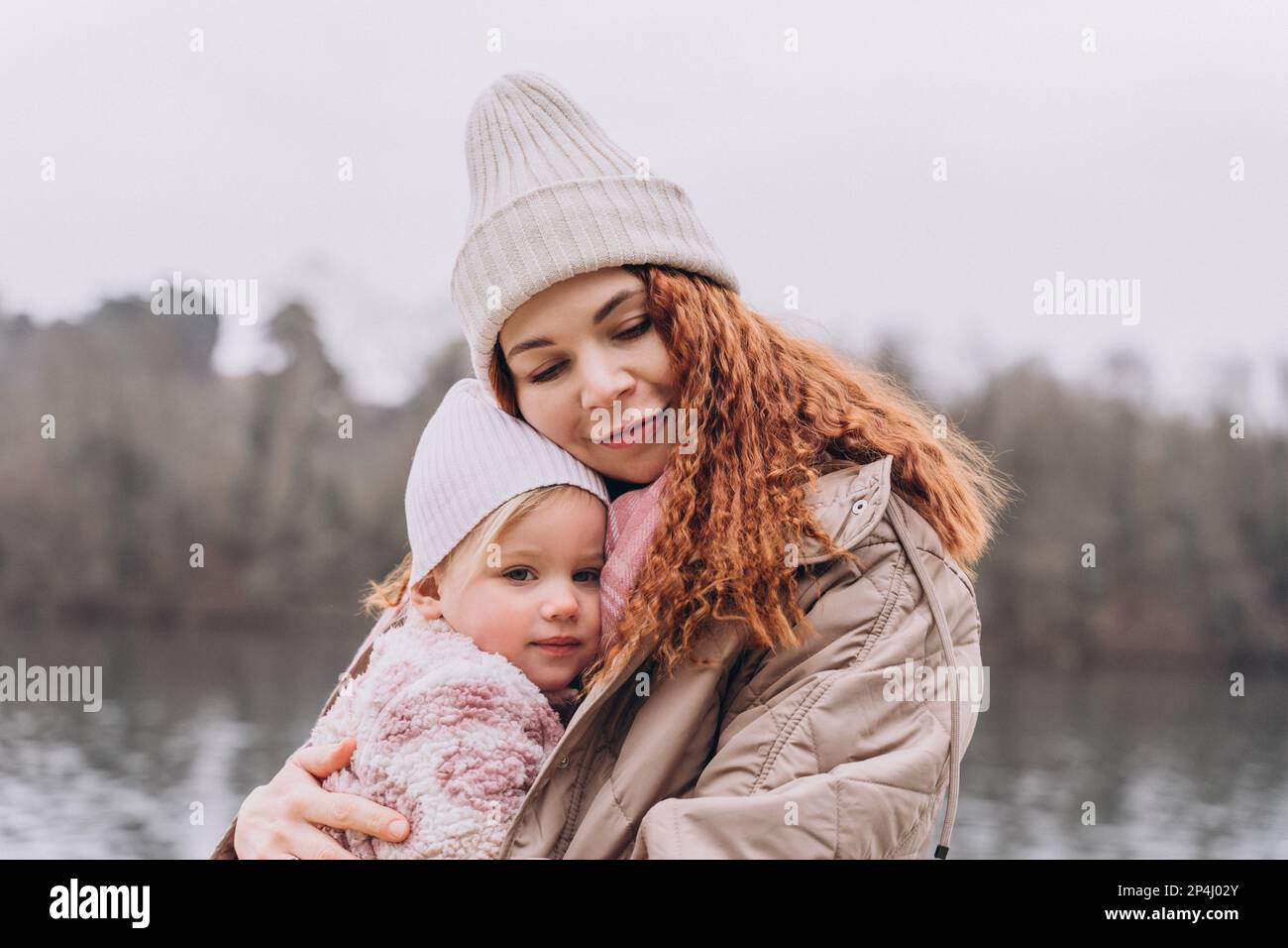 Curly mom and baby are sitting in a foggy park by the river hugging ...