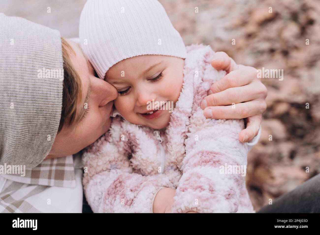 Dad hugs and kisses his two-year-old daughter outdoors in early spring ...