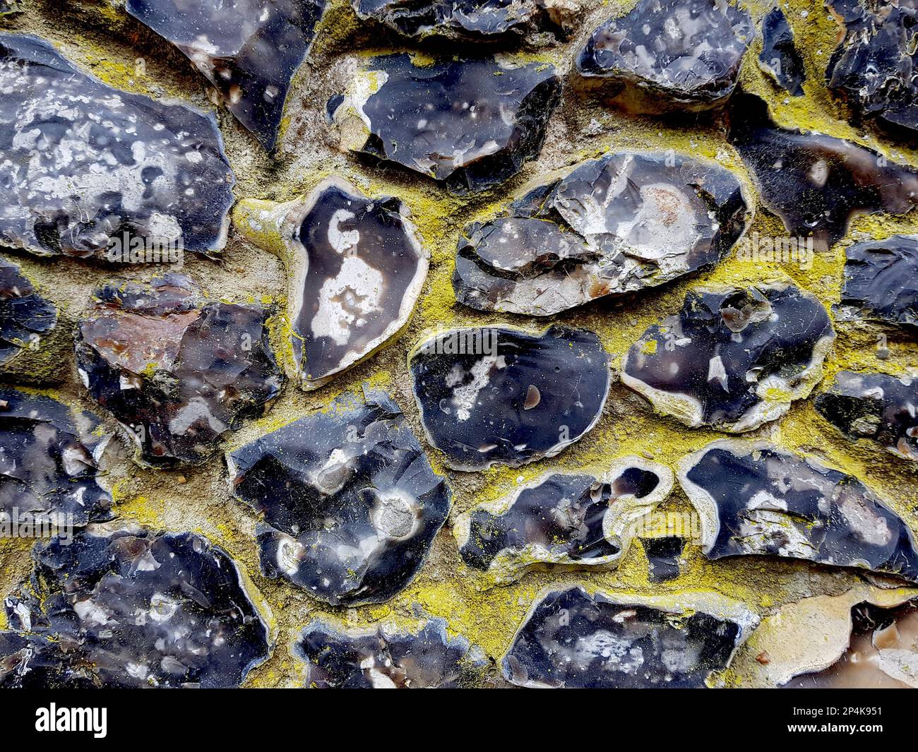 Detail of a black flint wall with yellow lichen Stock Photo - Alamy