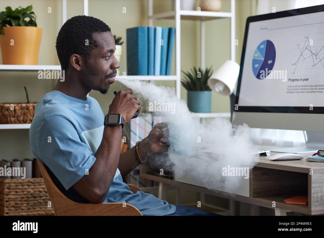 Side view of young businessman smoking e-cigarette and analyzing online ...