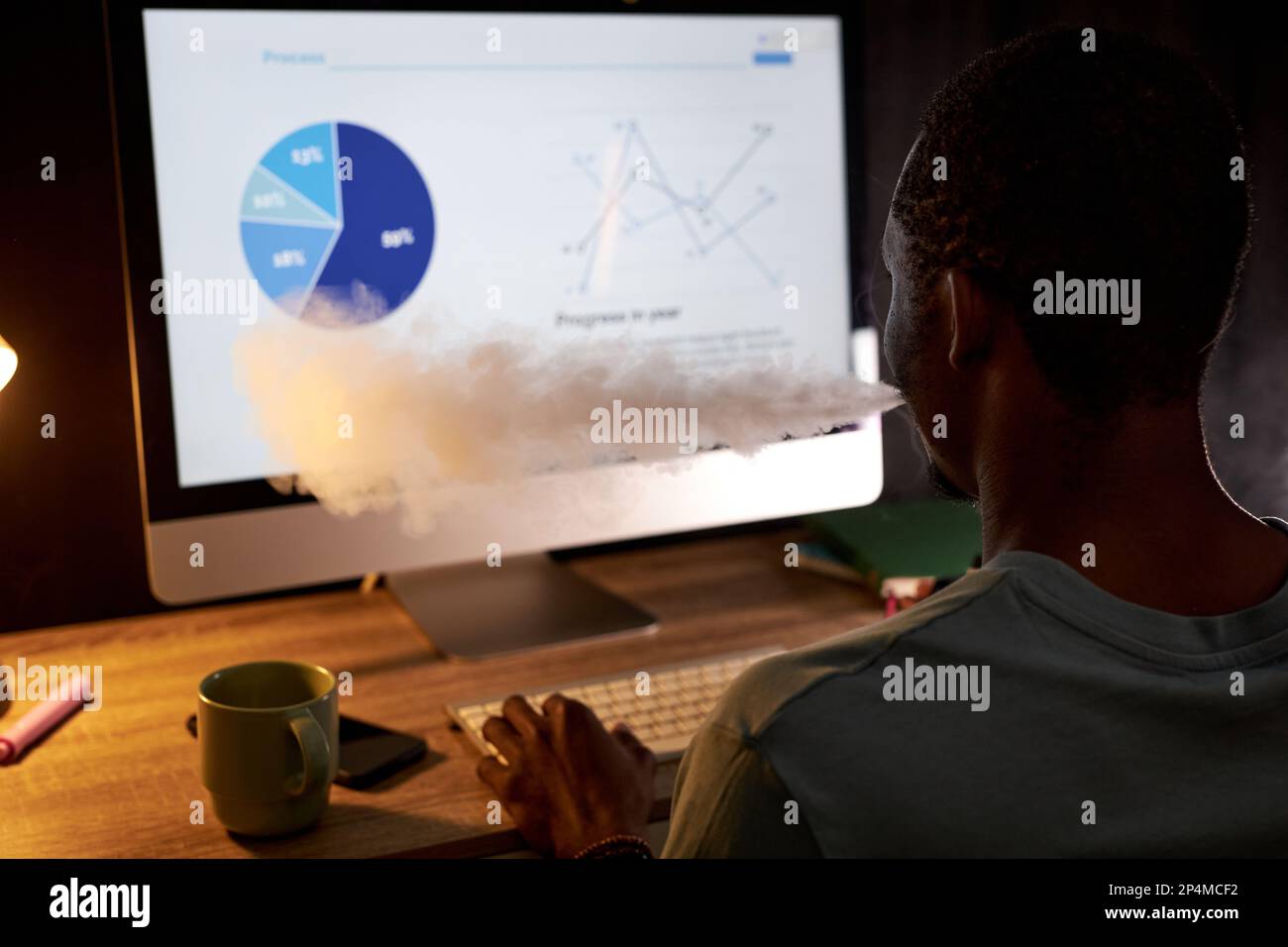 Young businessman smoking e-cigarette while sitting in front of ...