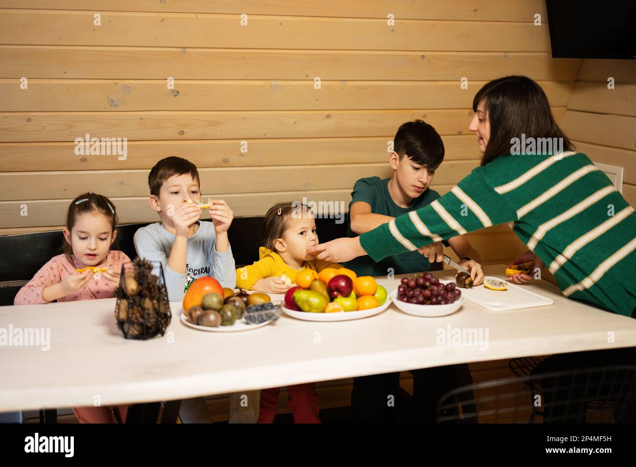 Mother with four children eat fruits in wooden country house on weekend ...