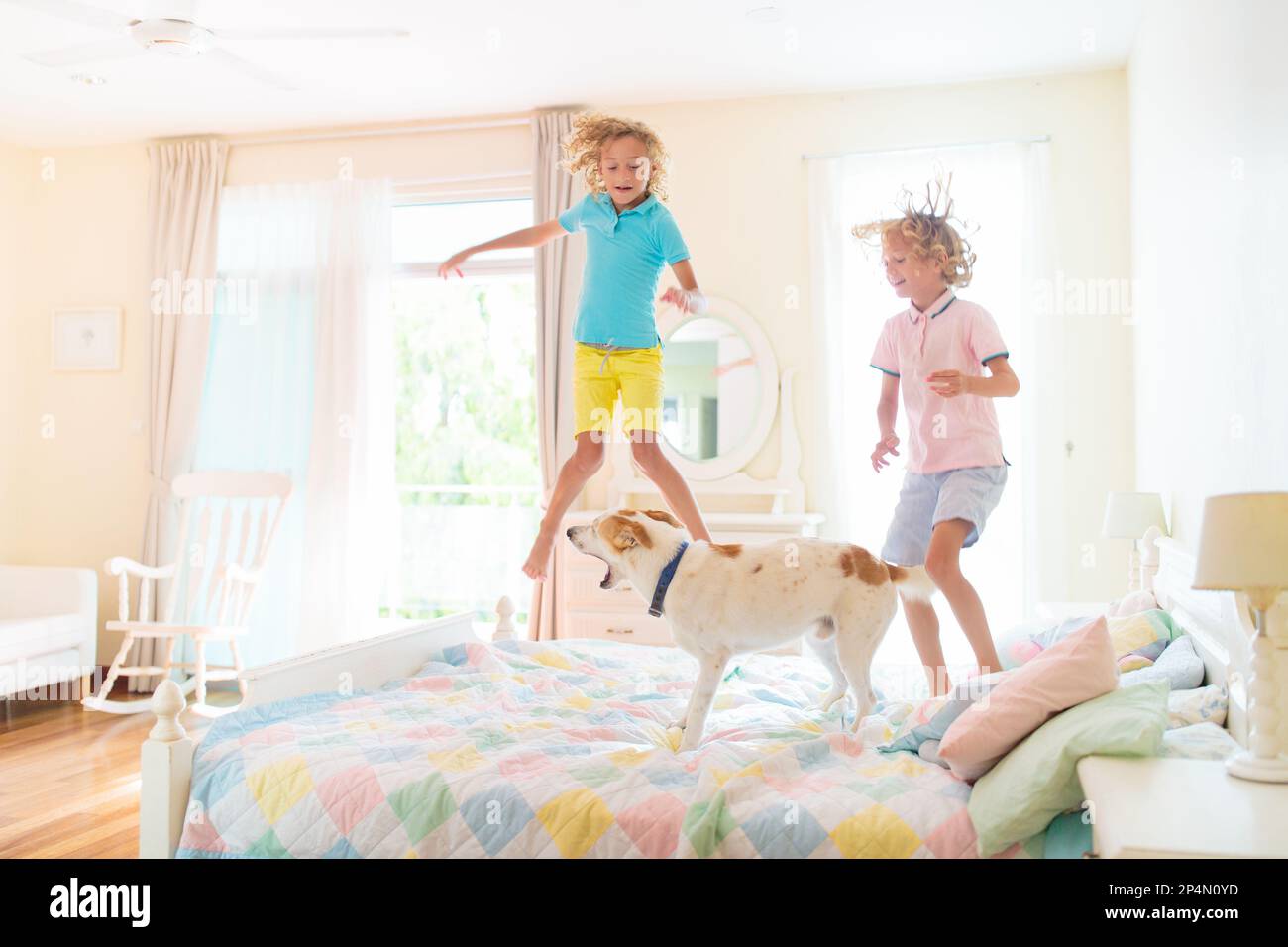 Child jumping on bed in white bedroom with big window. Kids play at ...