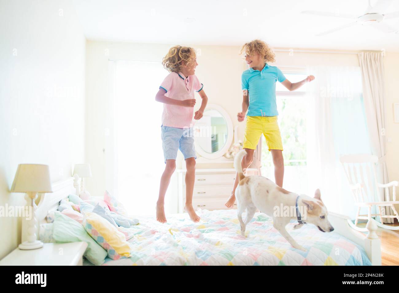 Child jumping on bed in white bedroom with big window. Kids play at ...