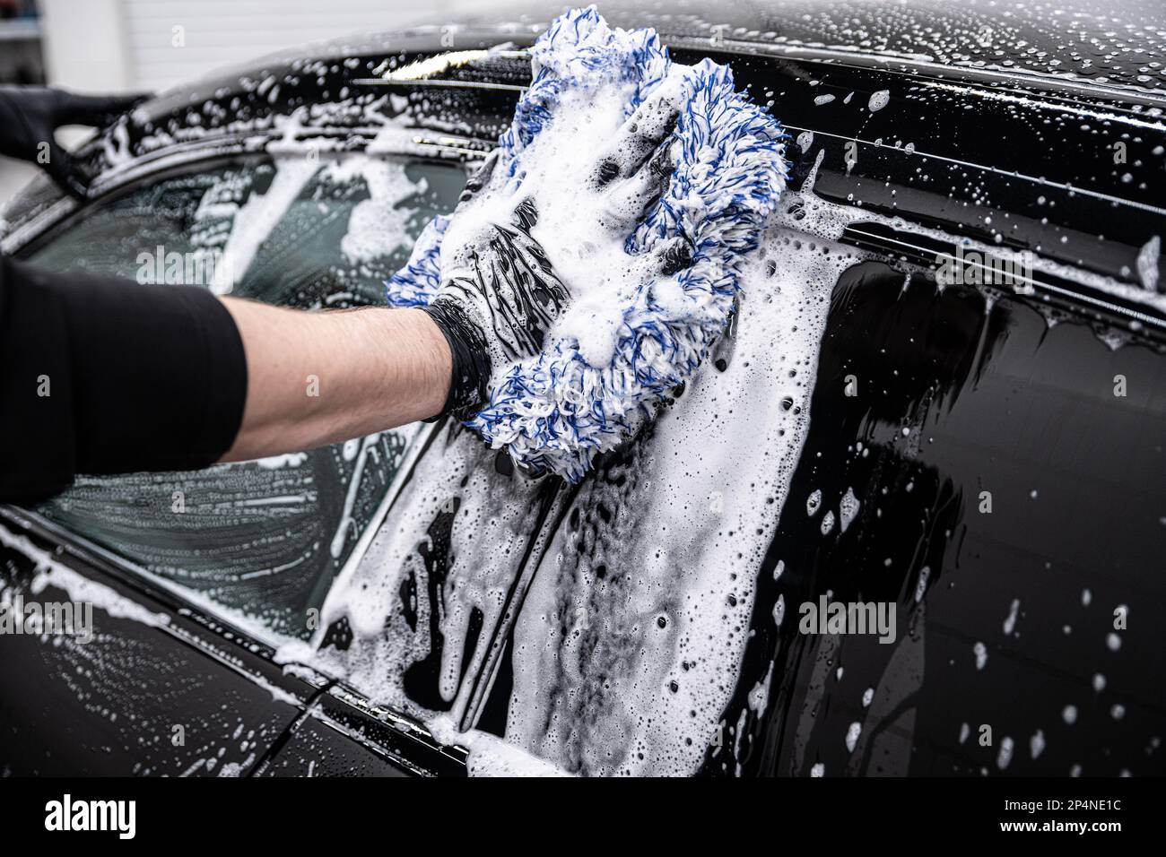 Employee of a car wash or car detailing studio carefully washes a car ...