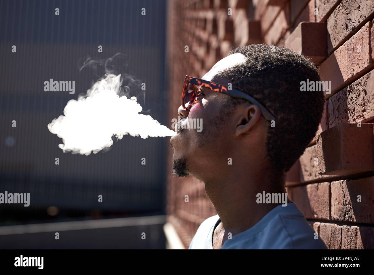 Side view of black man in sunglasses releasing cloud of white smoke out ...