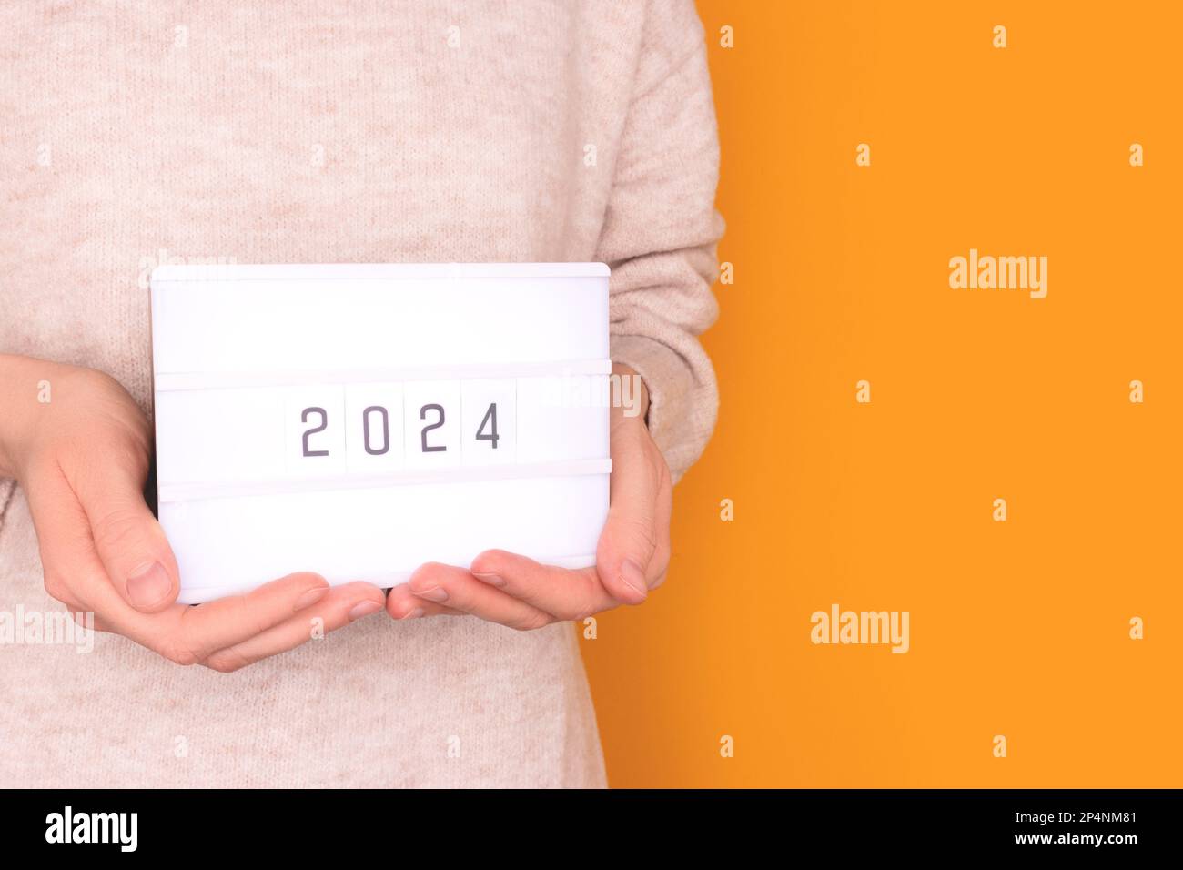 Female hands hold lightbox with 2024 numbers in front of yellow ...