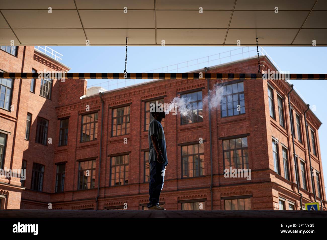 Side view of smoking young black man in casualwear standing against red ...