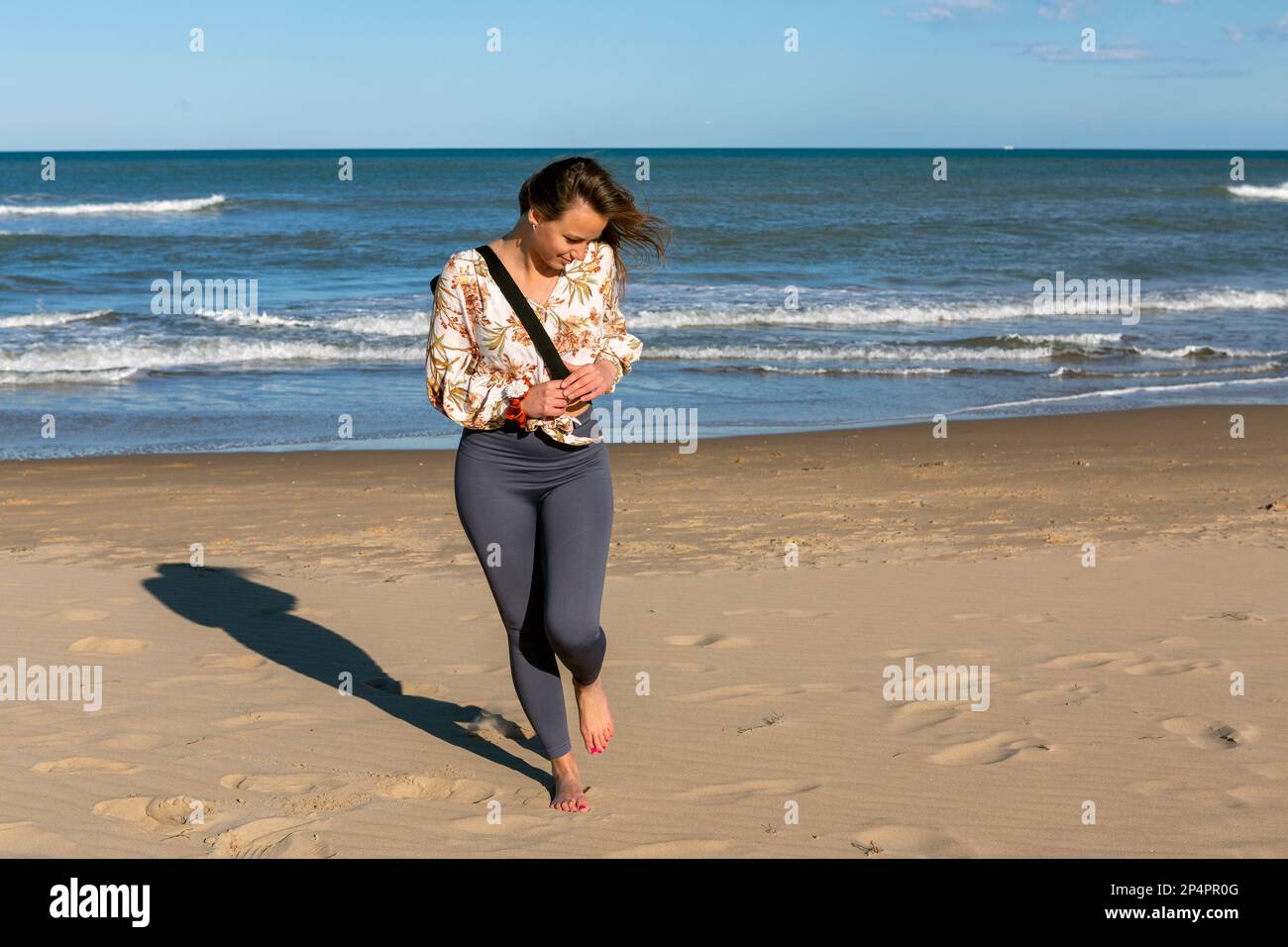 pretty woman walking barefoot on the beach with mat slung over her ...