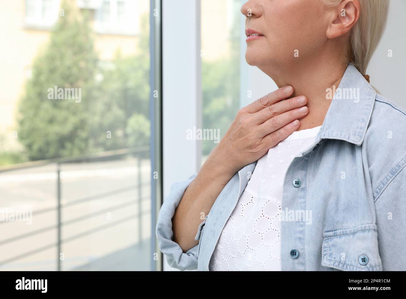 Mature woman doing thyroid self examination near window, closeup. Space ...
