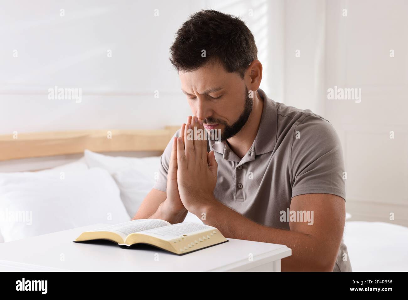 Religious man with Bible praying in bedroom Stock Photo - Alamy