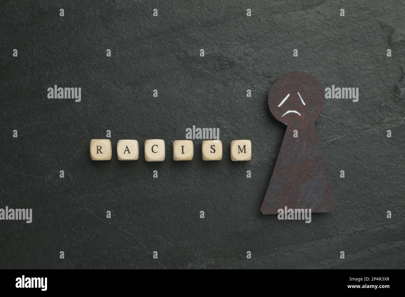 Word Racism and black paper figure with sad face on dark background ...