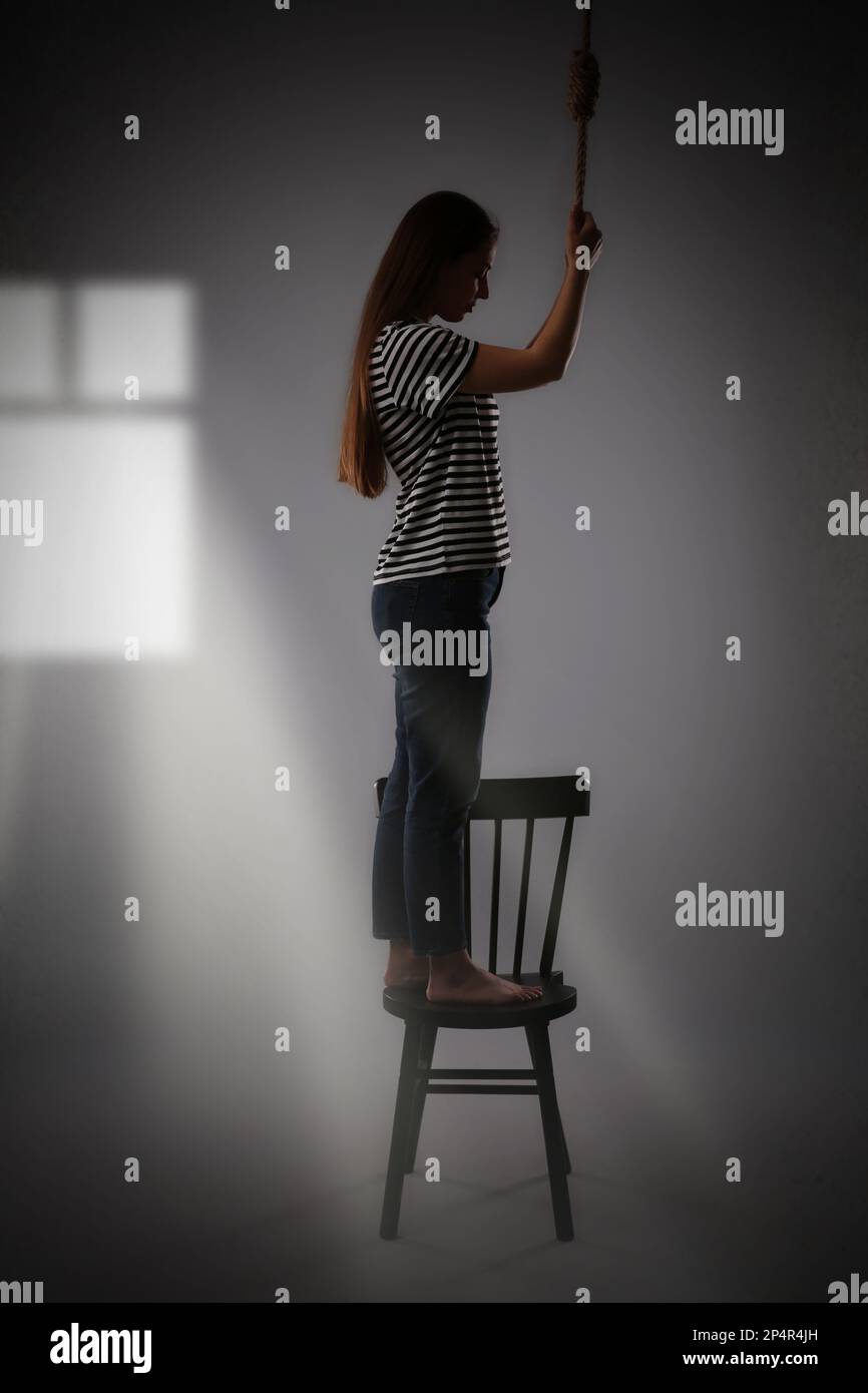 Depressed woman with rope noose standing on chair in room Stock Photo ...