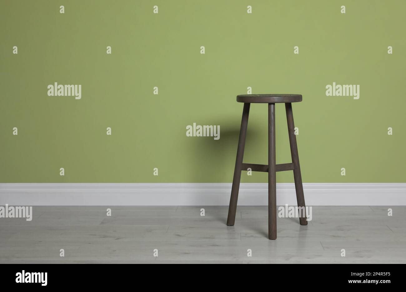 Stylish wooden stool near light green wall indoors. Space for text ...