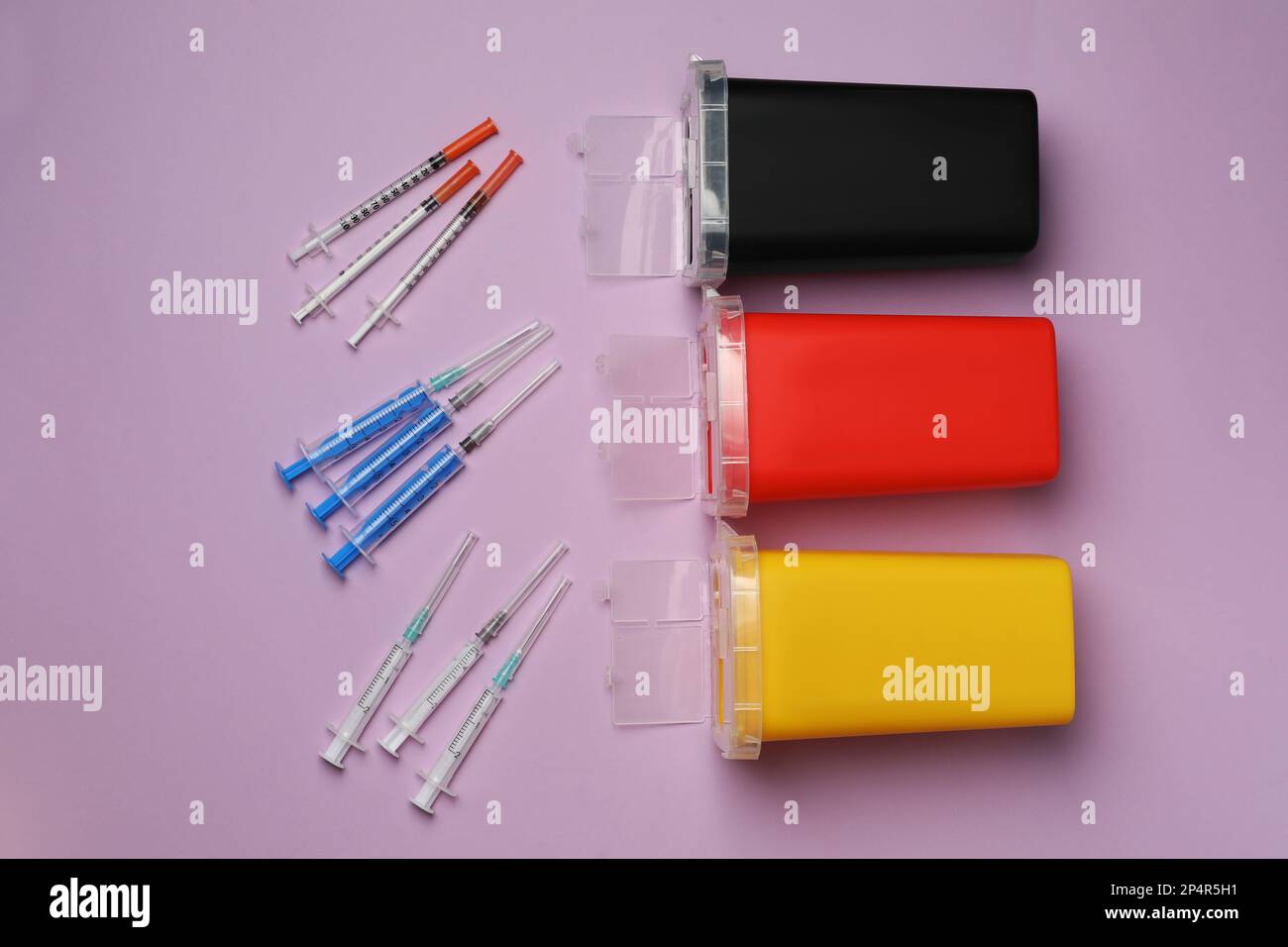 Disposable syringes with needles and sharps containers on violet ...