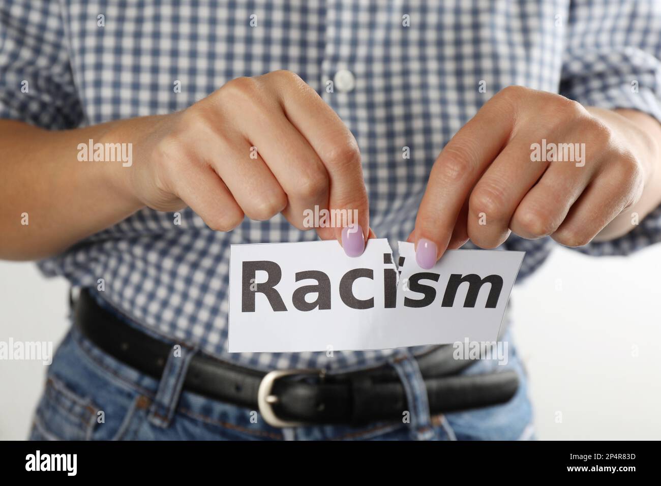 Woman tearing up paper sheet with word Racism on white background ...