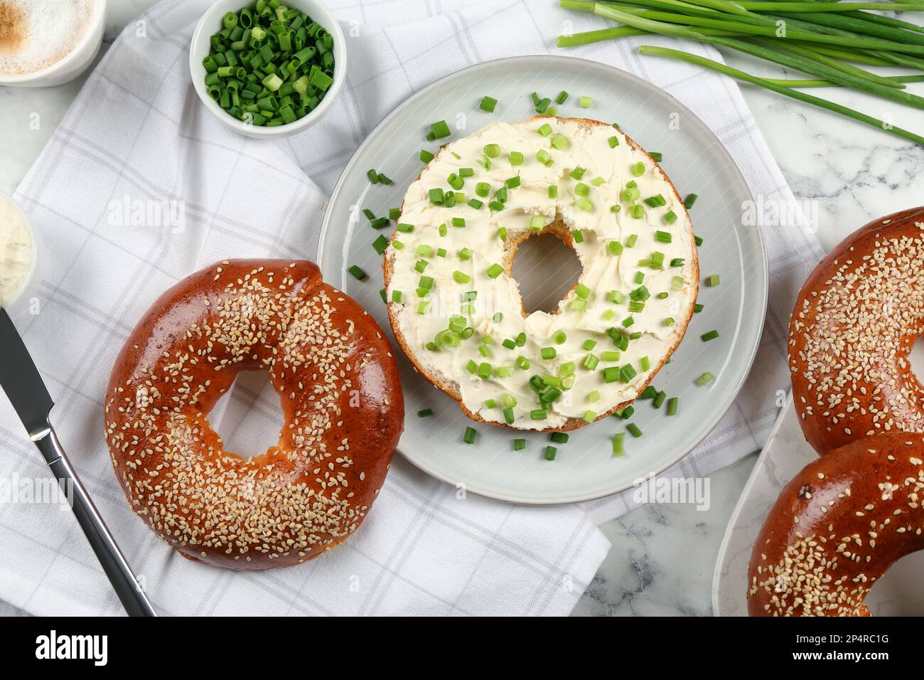 Delicious bagel with cream cheese and green onion on white marble table ...