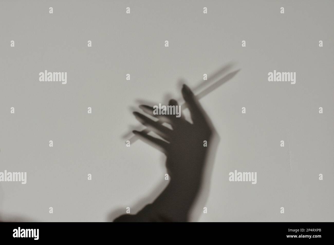 Shadow of the female hand holding a pencil , sign on the light wall ...