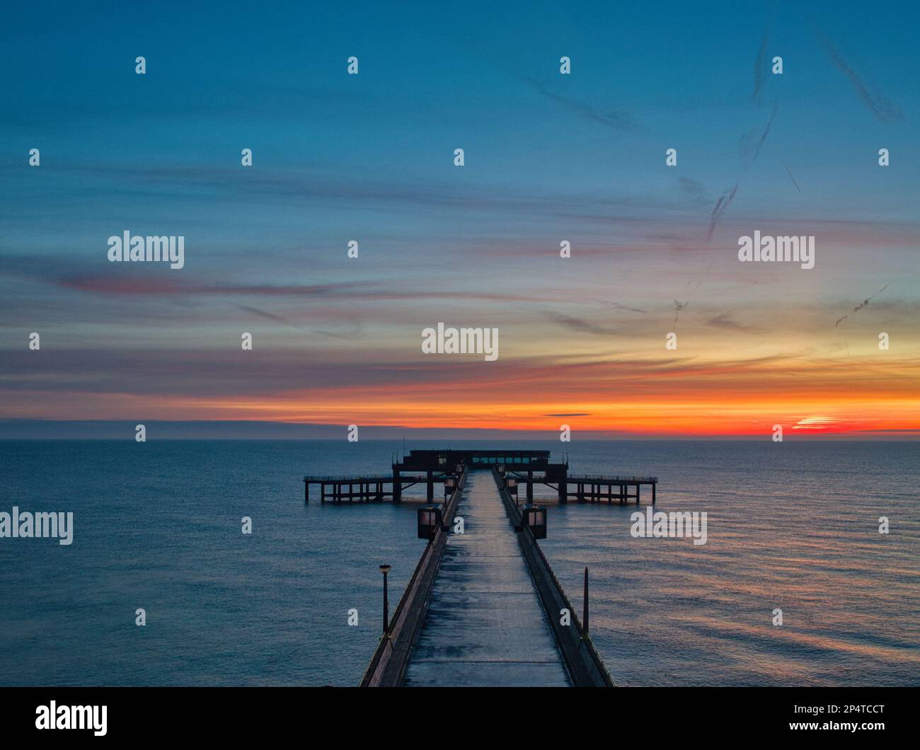 A scenic dock extending out into the glistening ocean at a sunset hour ...