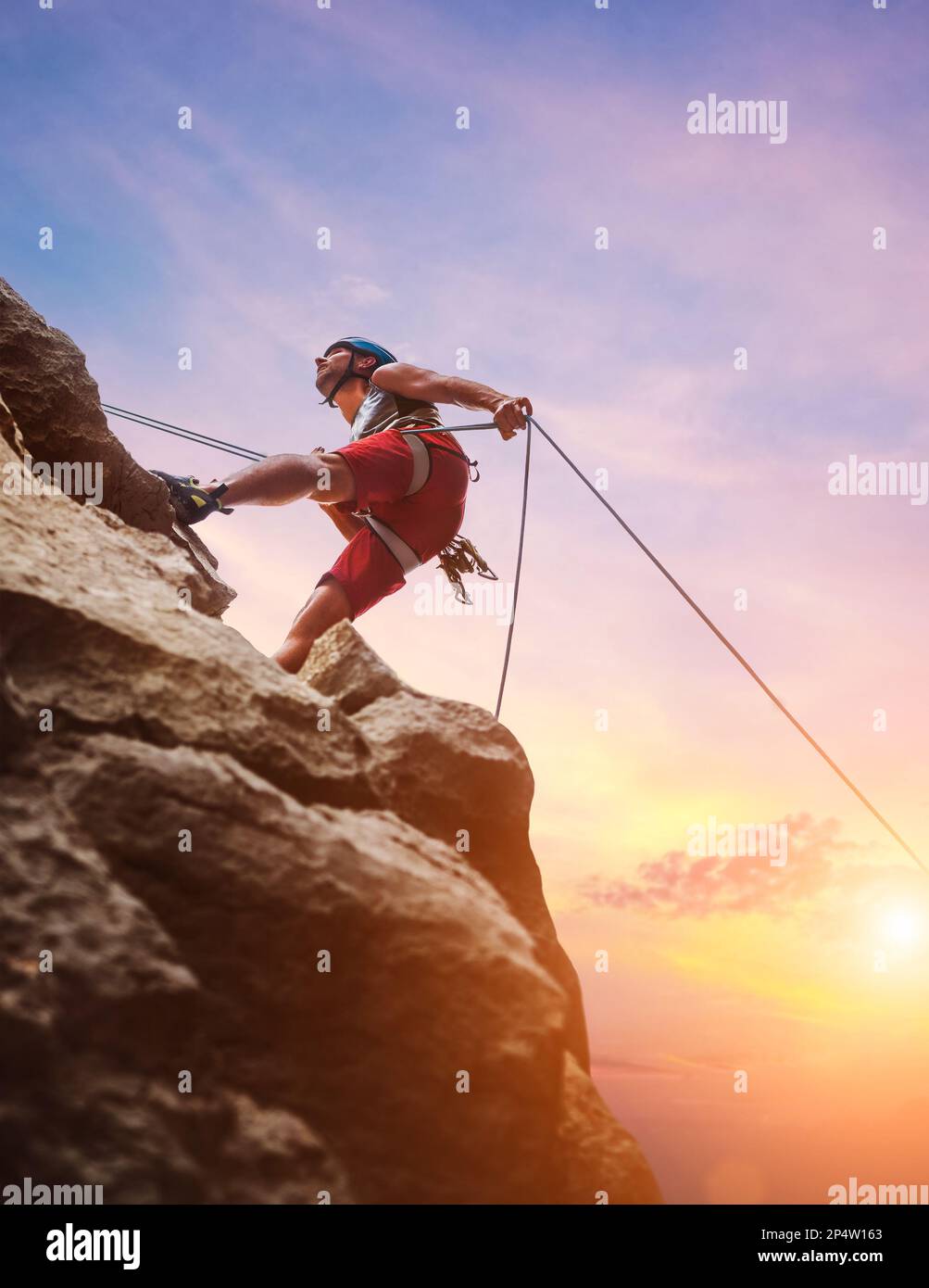 Muscular climber man in protective helmet abseiling from cliff rock ...