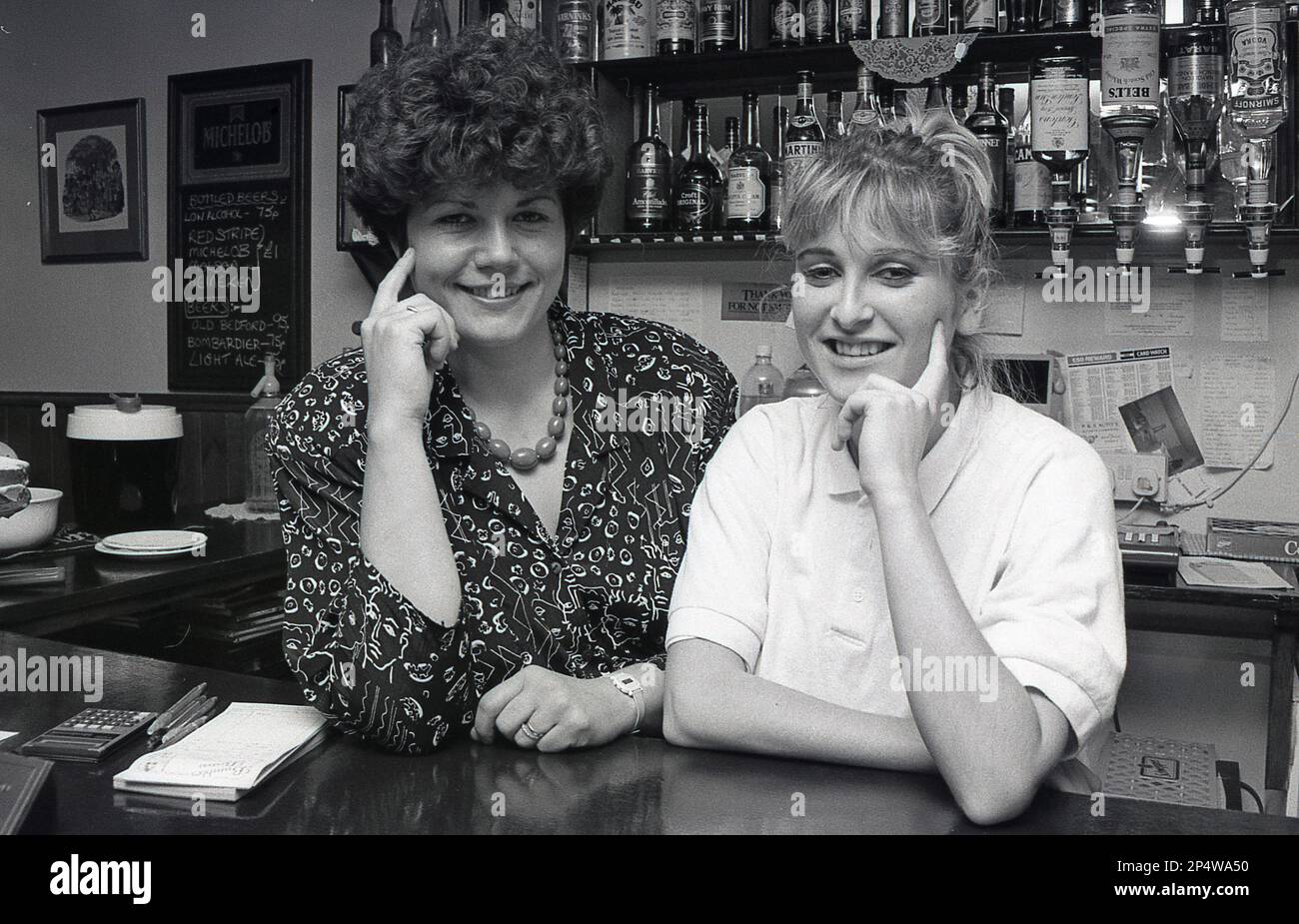 1980s, two young female bar staff posing for their photo behind the bar ...