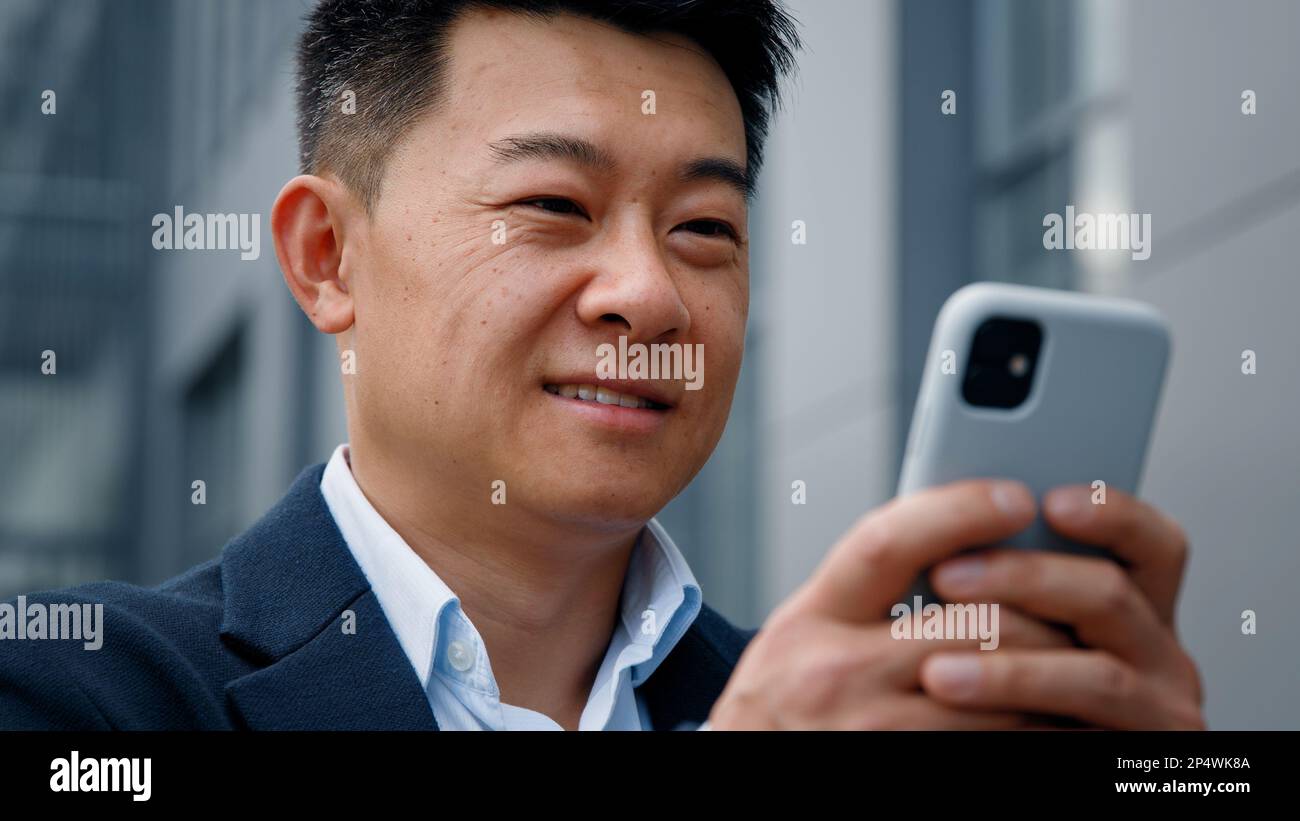 Happy male in city outdoors looking phone screen Asian 40s businessman ...