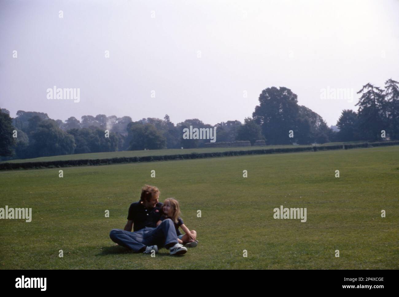 A dad sitting with his 5 year old daughter in the park, in the 1970s in ...