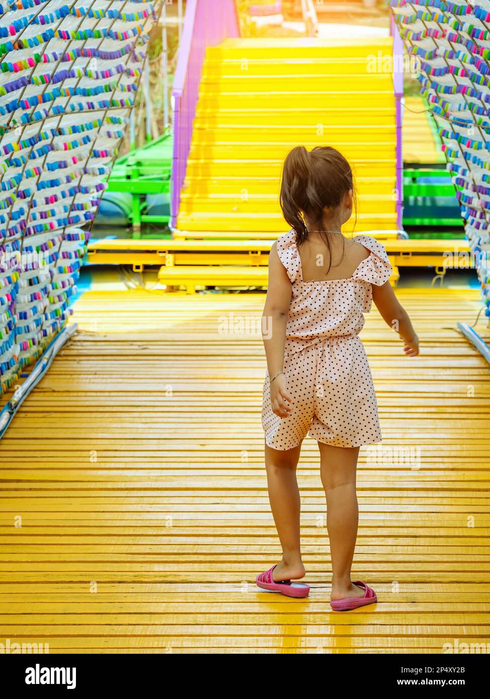 Back view of Asian little girl walk across yellow wooden bridge with ...