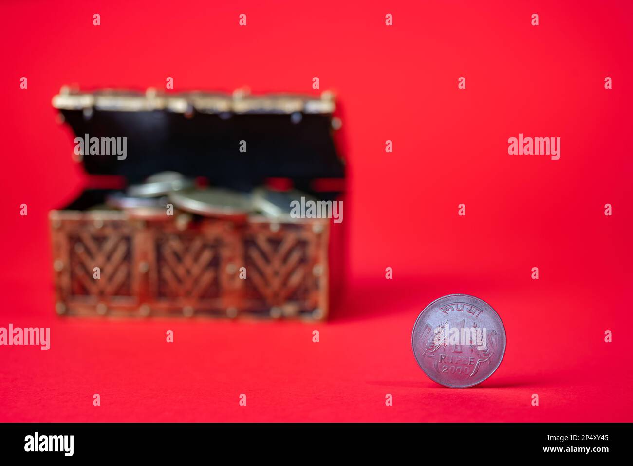 Rupee coin standing on the table, red backdrop. Blurred bank vault full ...